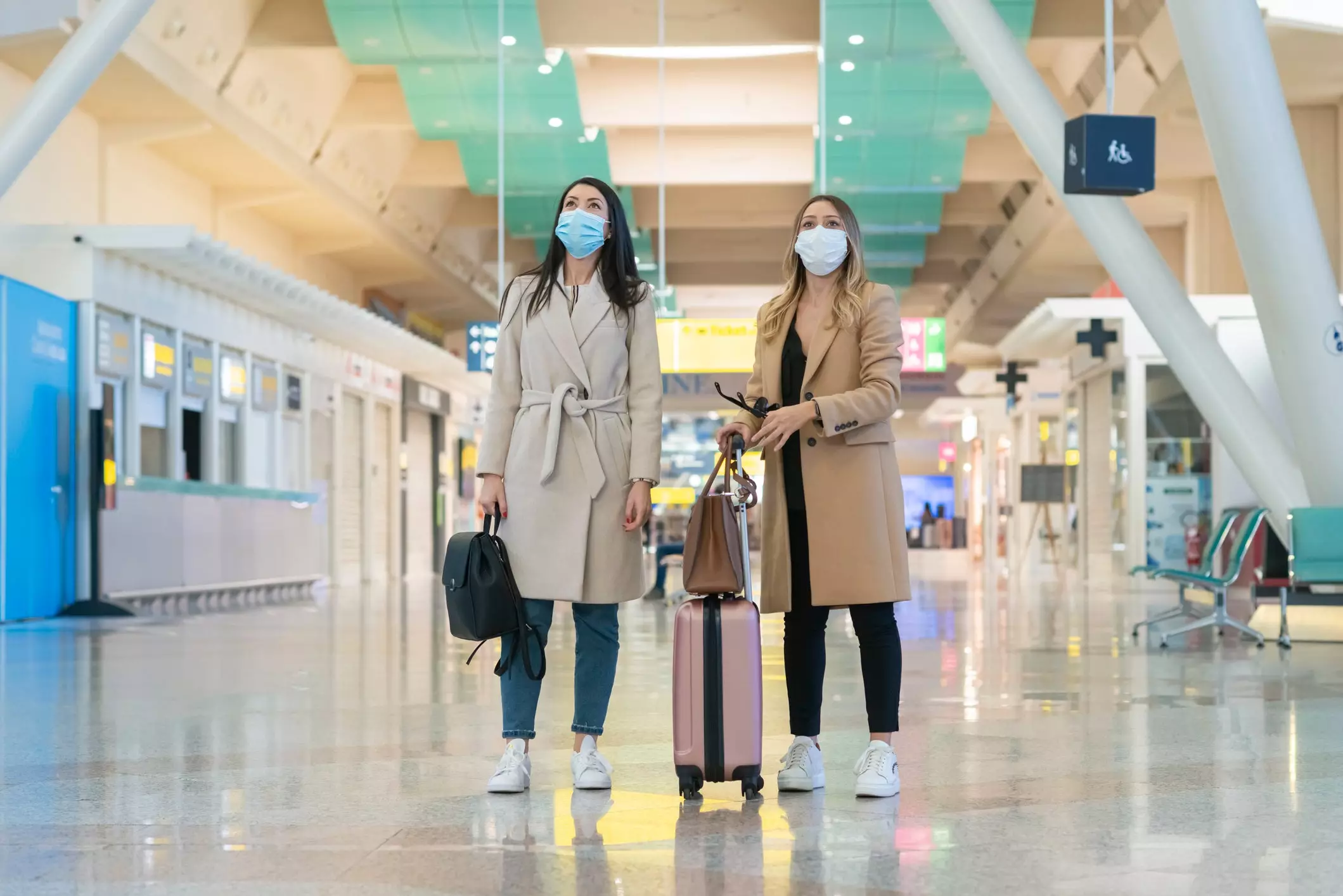 To unge kvinner som bærer masker mens de venter sammen på en flyplass (Foto: Francesco Carta fotografo/Getty Images)