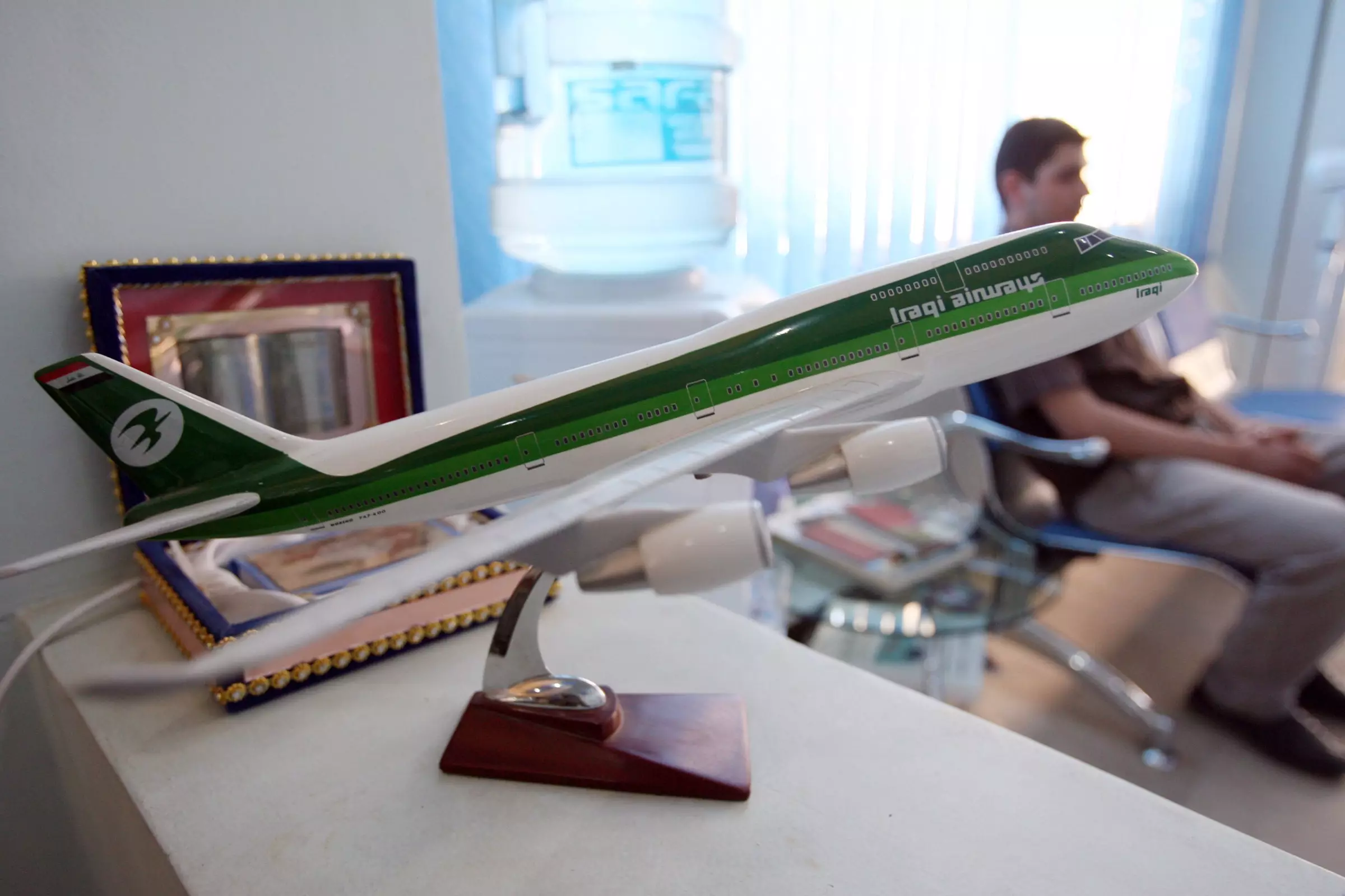 Un modelo de avión se sienta en un escritorio mientras los clientes esperan en una oficina de Iraqi Airways en Bagdad el 26 de mayo de 2010. Bagdad ha decidido cerrar la propiedad estatal de Iraqi Airways ante una disputa financiera de décadas con el vecino Kuwait que provocó la incautación de uno de sus aviones el mes pasado, anunció el Ministerio de Transporte. AFP PHOTO/ALI AL-SAADI (El crédito de la foto debe decir ALI AL-SAADI/AFP vía Getty Images)