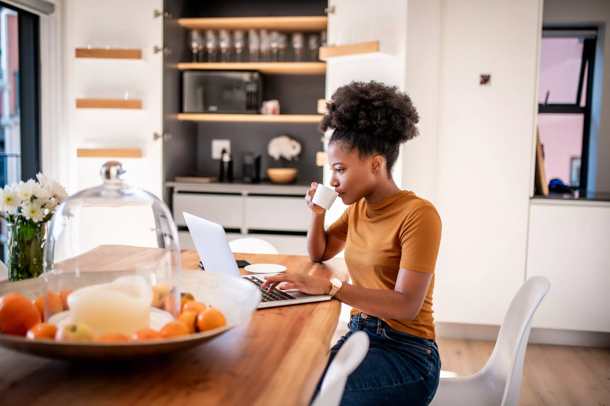 Mara tixrob il-kafè waqt li tuża laptop fil-kċina