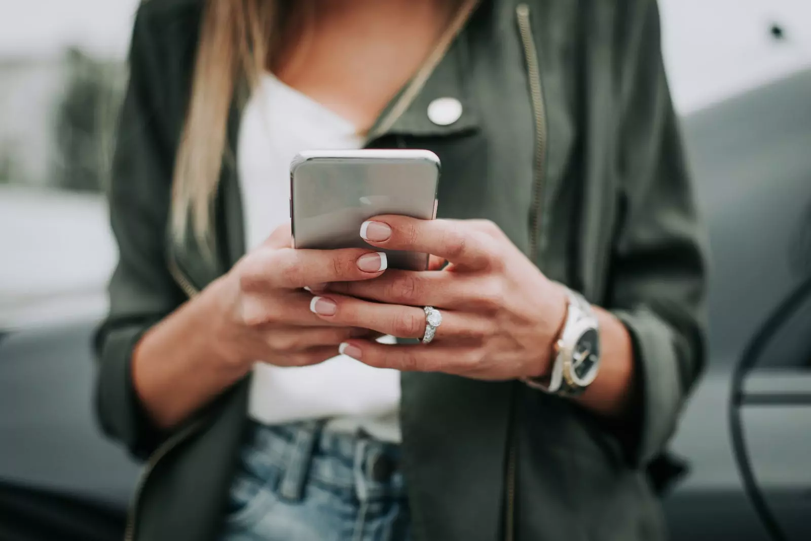 Ženska roka od blizu pošilja sporočilo po telefonu, medtem ko nosi sodobno uro in prstane