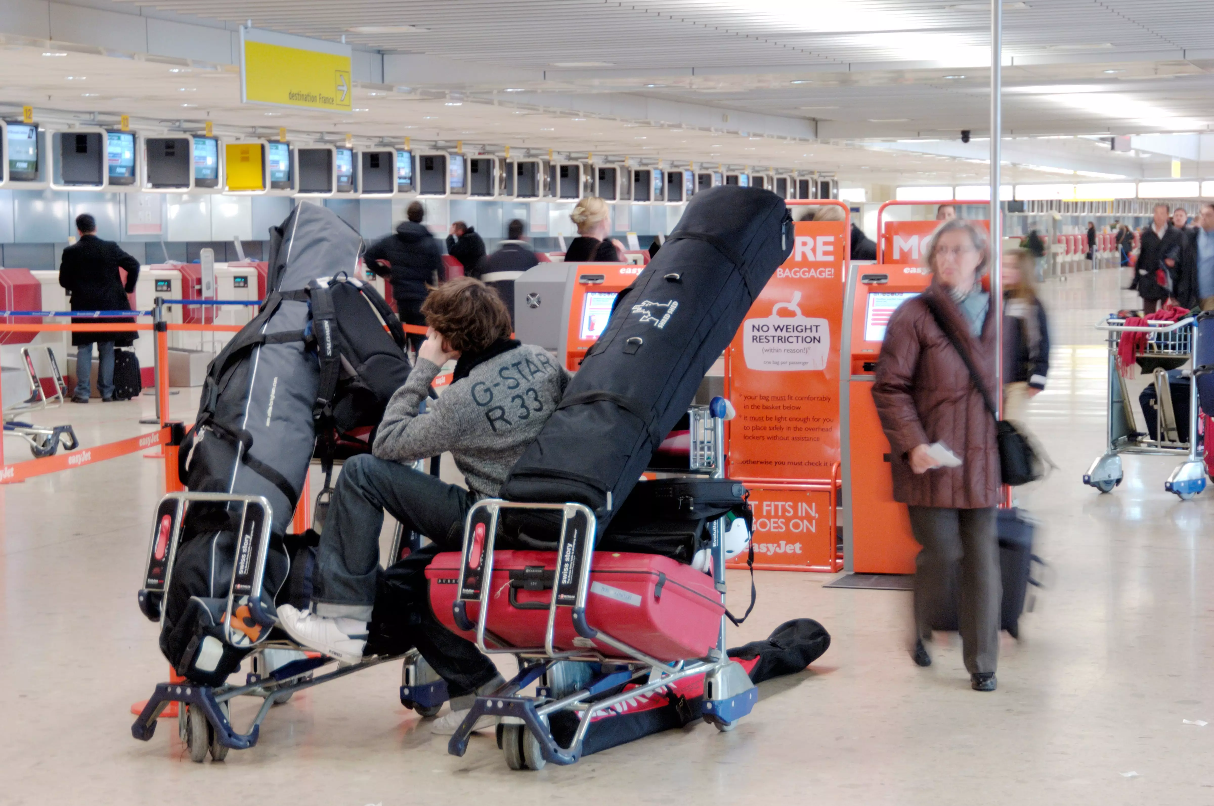 wong lungguh ing troli bagasi kebak bagasi lan ski ing area check-in easyJet. (Foto: aviation-images.com/UIG liwat Gambar Getty)