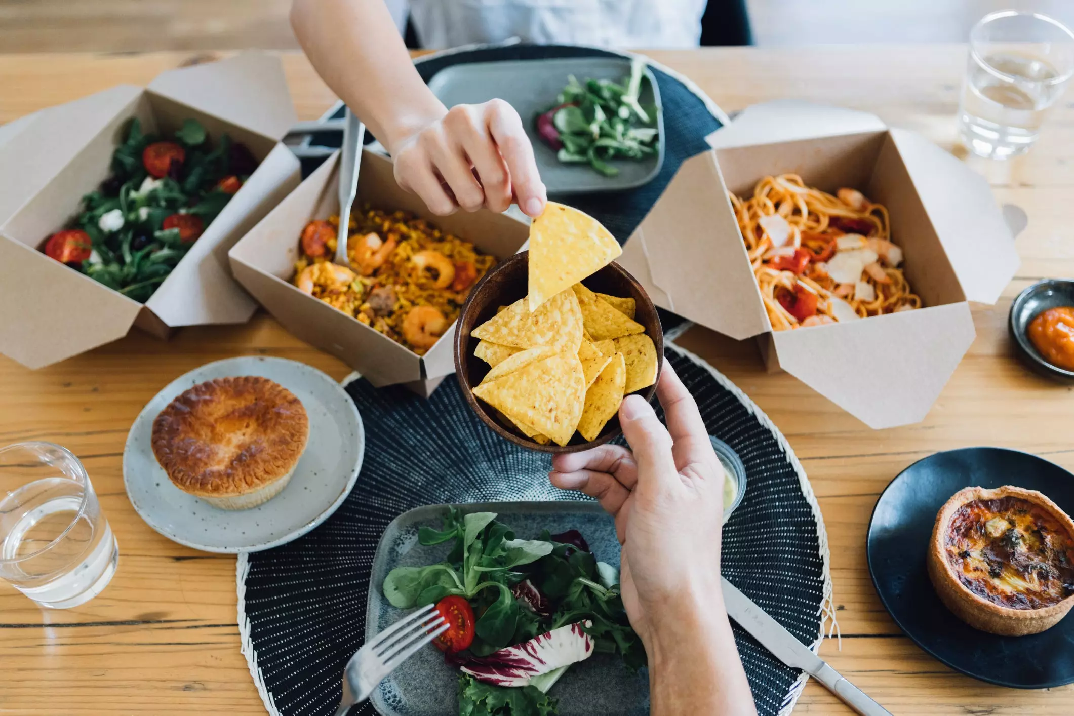 Pandangan perspektif peribadi pasangan berkongsi kerepek Tortilla sambil makan makanan bawa pulang bersama-sama di meja makan.