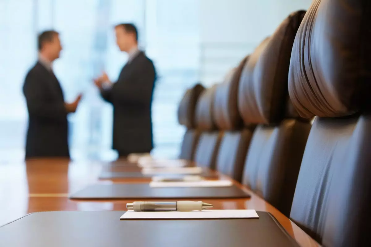 Mesa de la sala de conferencias con sillas de cuero y dos hombres de traje parados al fondo