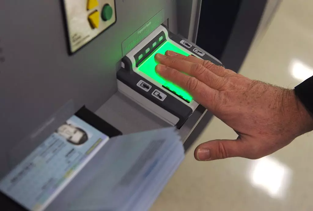 Amalungu e-Global Entry afaka amaphasipoti awo, athathwe izithombe bese kuskenwa izigxivizo zeminwe njengengxenye yenqubo yokungenela. (Isithombe nguKatherine Frey / The Washington Post / Getty Images)